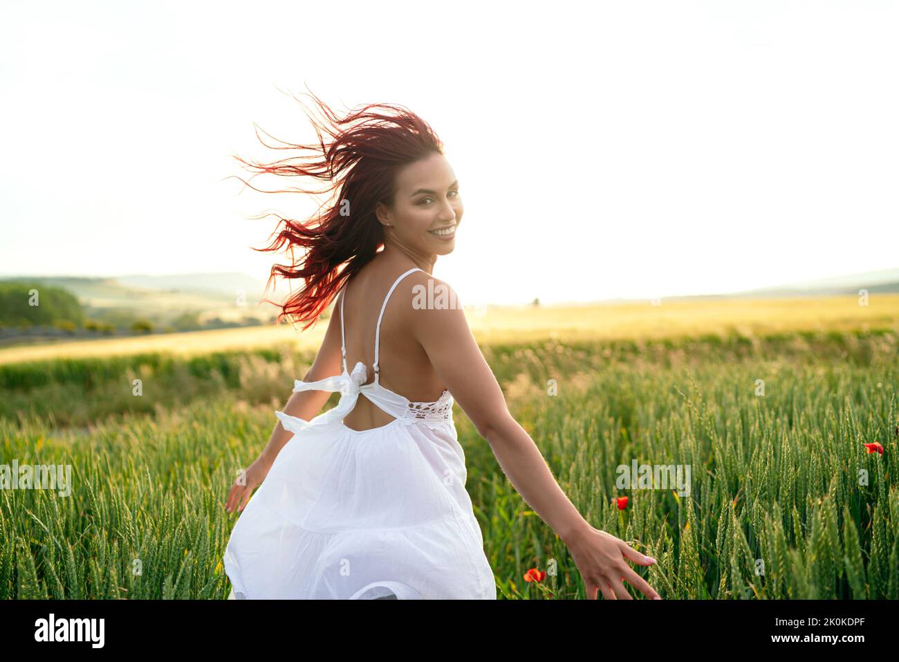 Back view of cheerful young female in sundress with red hair looking at ...