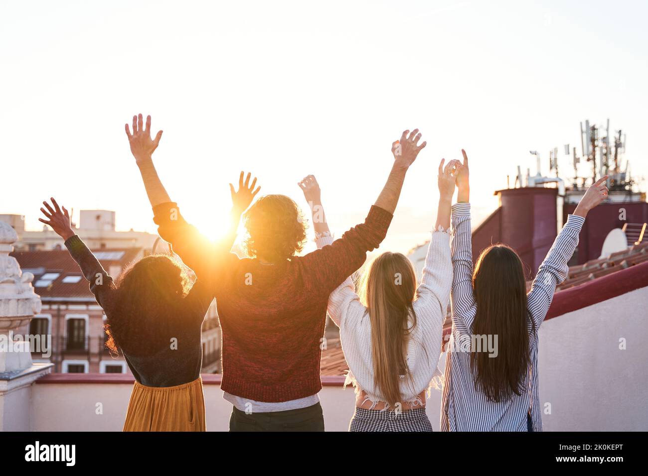 Back view faceless excited friends with arms raised in back lit wearing ...
