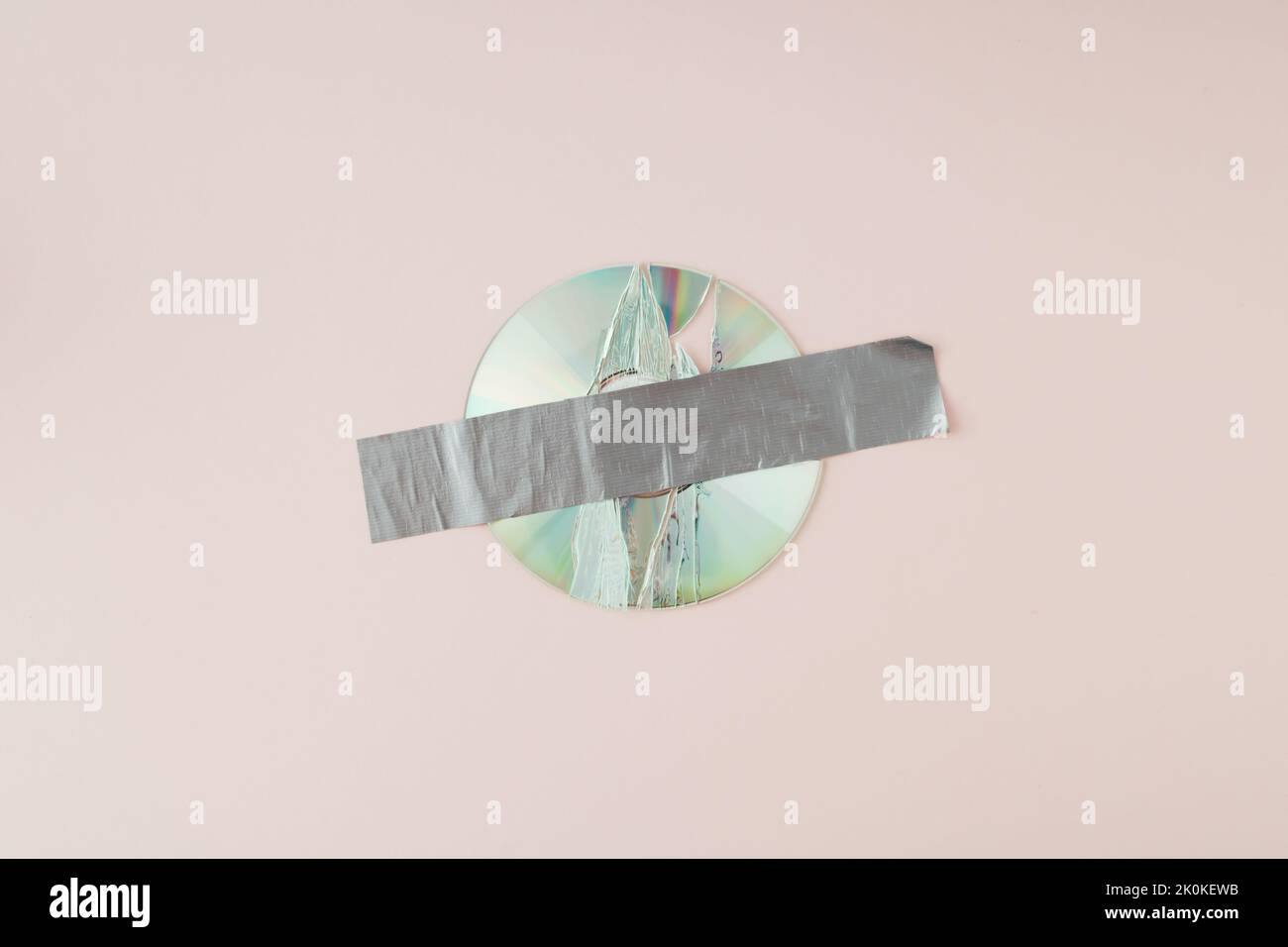 Broken digital audio compact disc tapped with gray duct tape on pink ...
