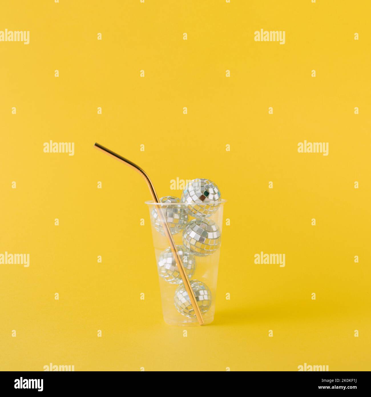 Transparent plastic cup filled with disco balls and golden metal straw ...