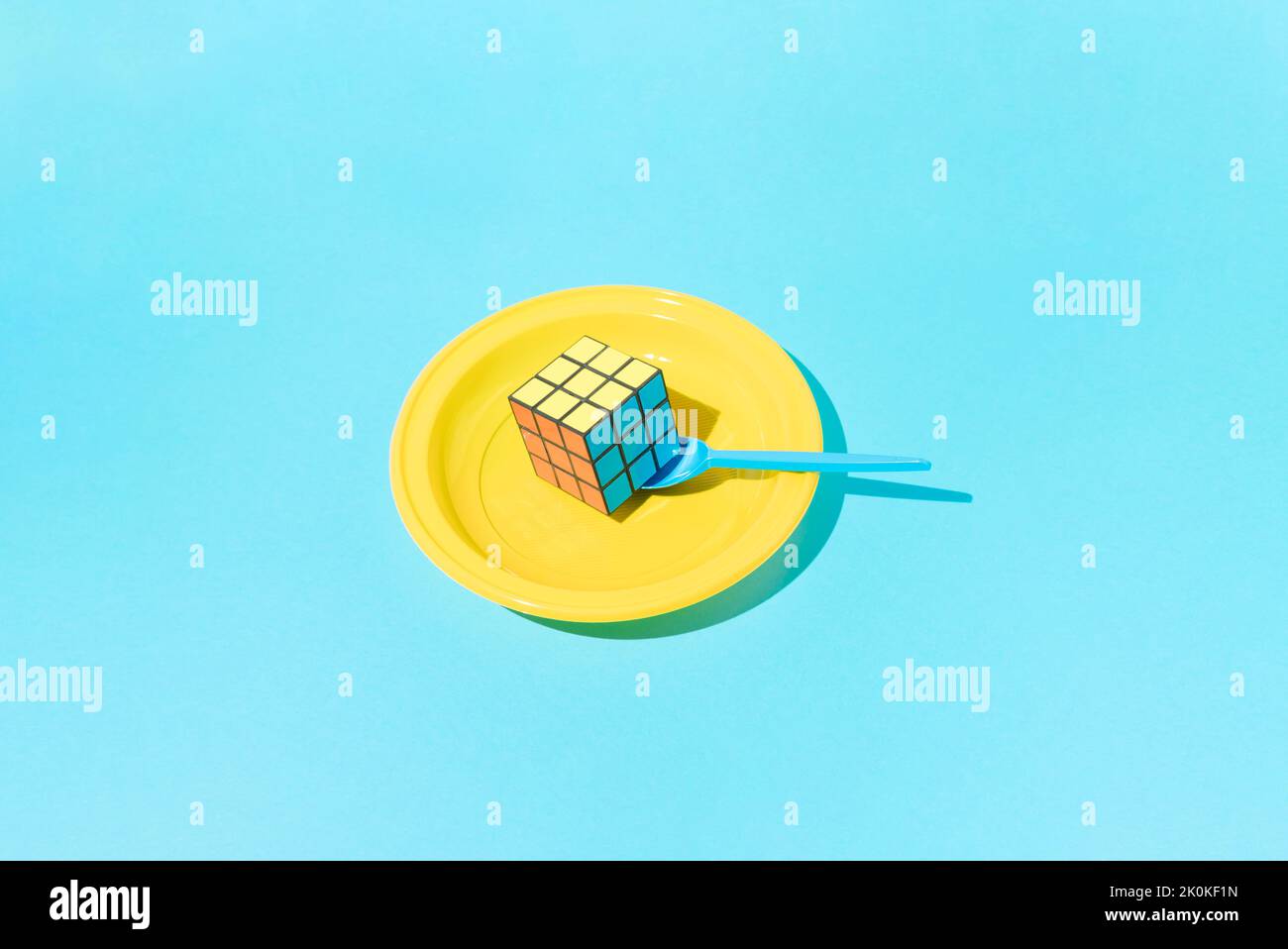 Yellow plastic plate with puzzle cube and blue plastic spoon on blue ...