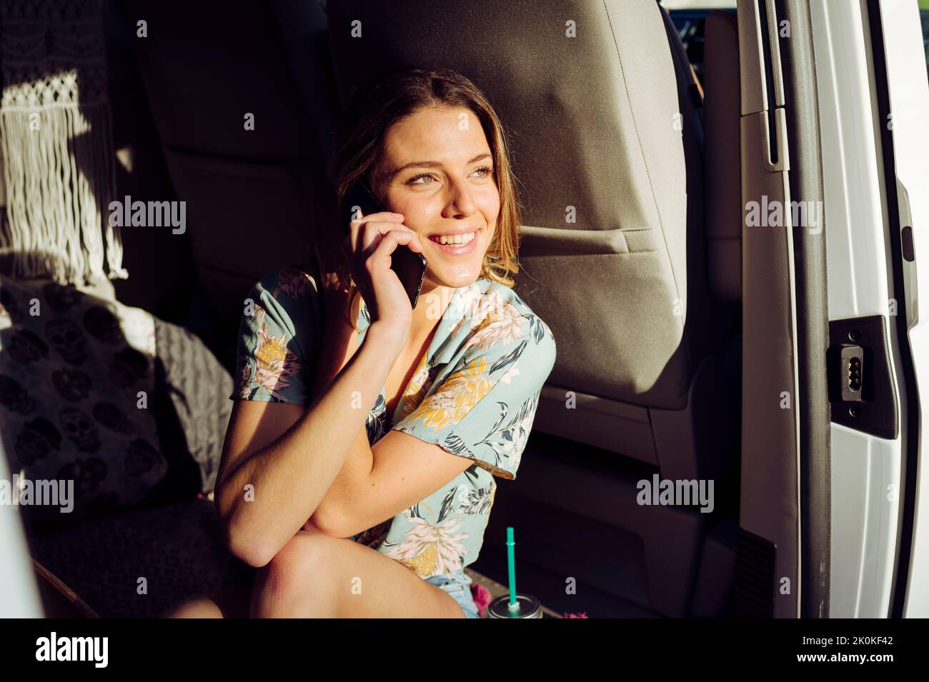 Blonde pretty woman into a minivan using her smartphone with sun ...