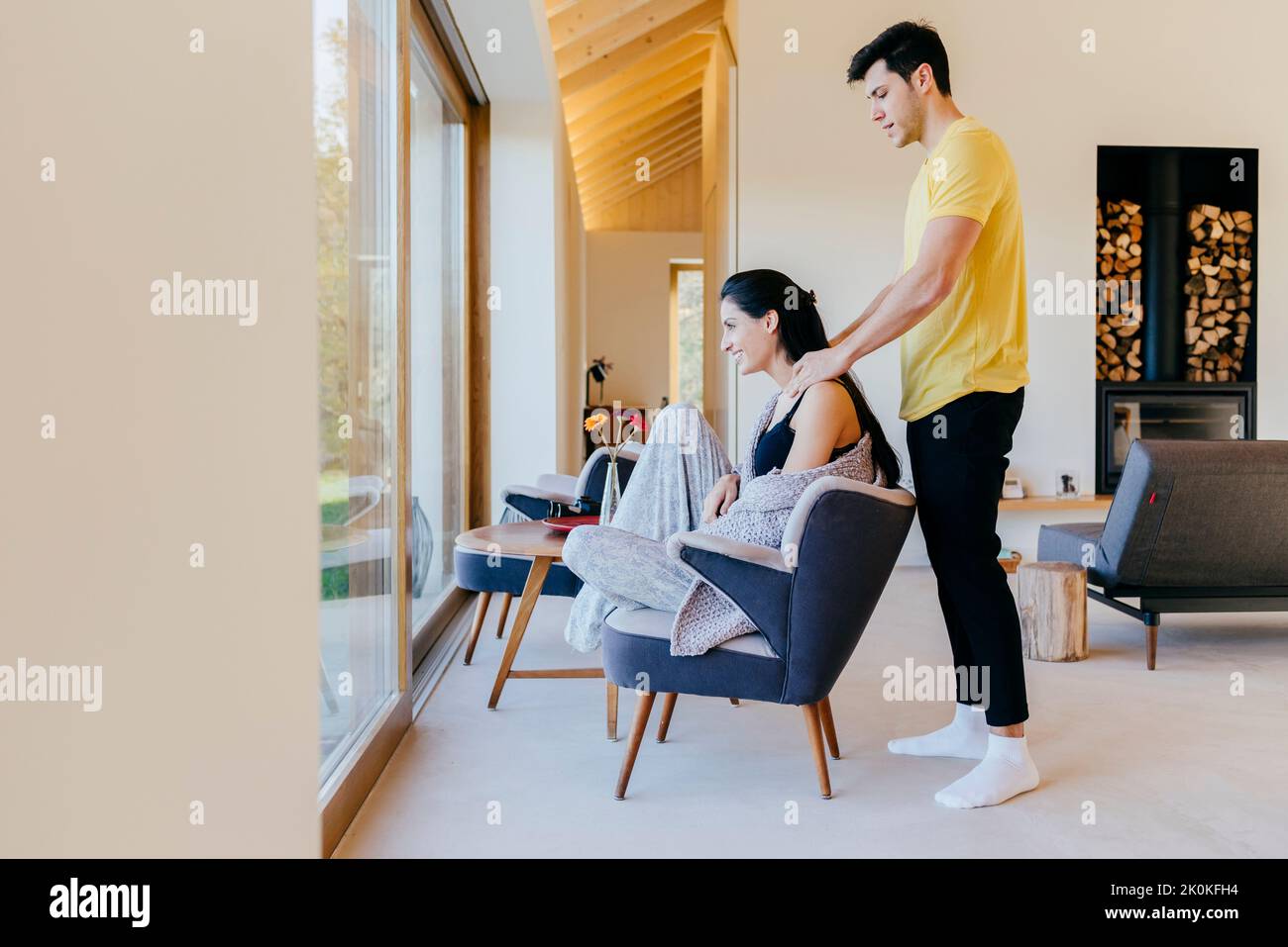 Young man giving a massage to girlfriend on chair in room and looking ...