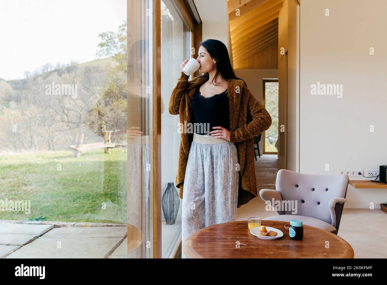Attractive Hispanic lady with mug of drink standing and looking at big ...