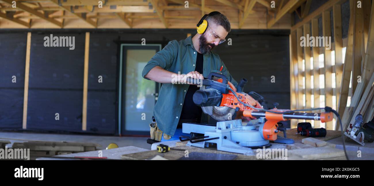 Construction worker working with eletric saw inside wooden construction ...