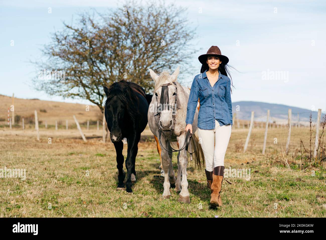Beautiful smiling brunette in boots and denim shirt walking on ranch ...