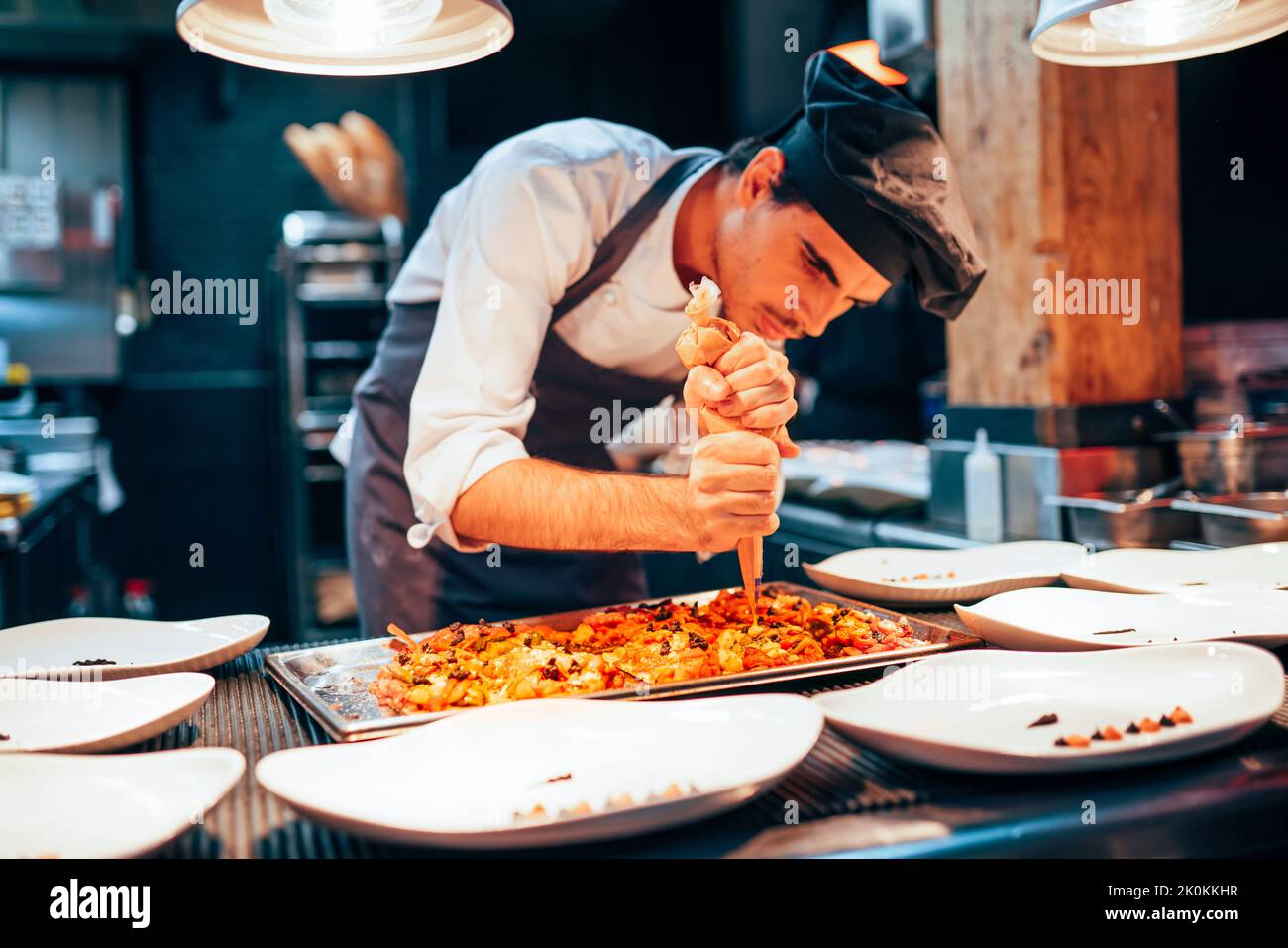 Side view of man in hat serving meal in restaurant kitchen pouring ...