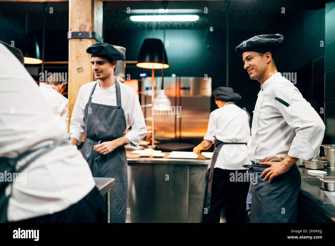 Men in hats and aprons working in team and serving dishes with ...