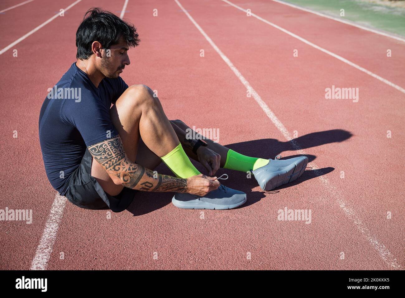 Side view of Hispanic male runner sitting on racetrack and tying ...