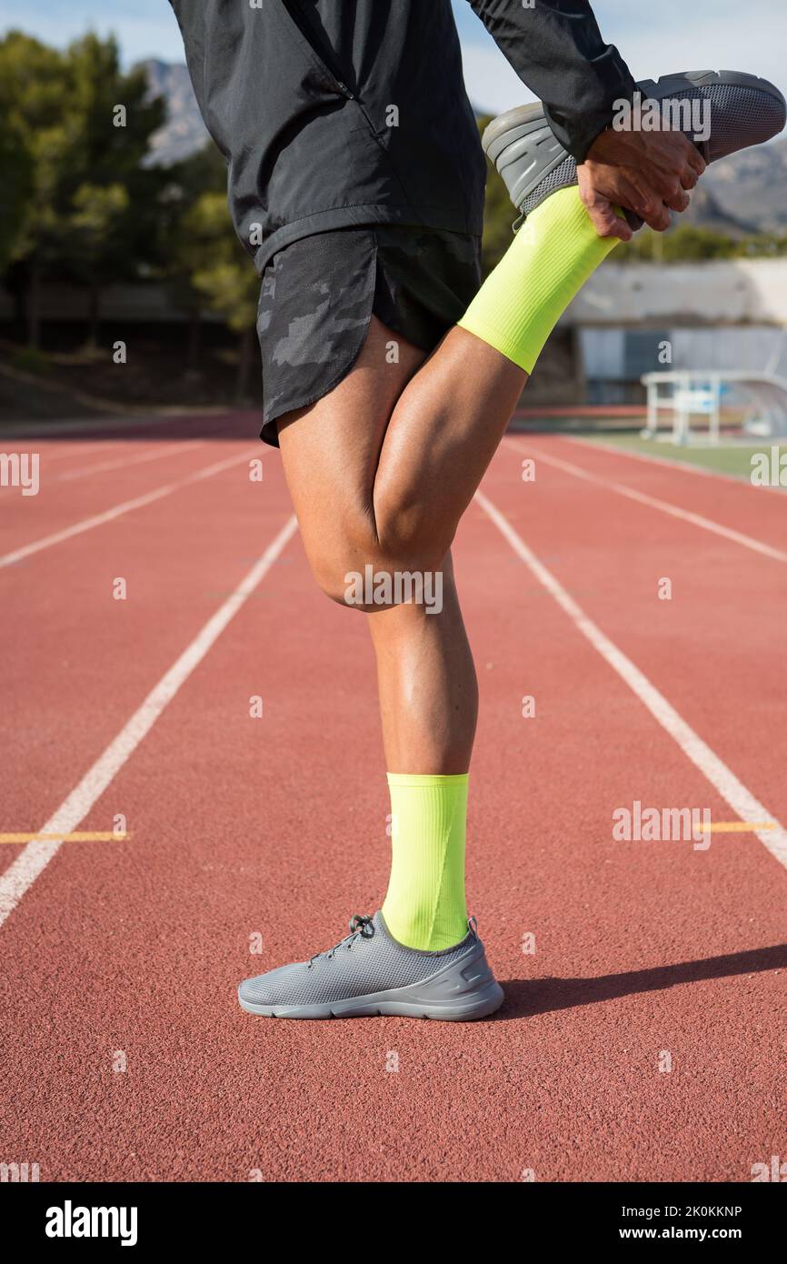 Determined Hispanic male runner stretching legs while warming up before ...