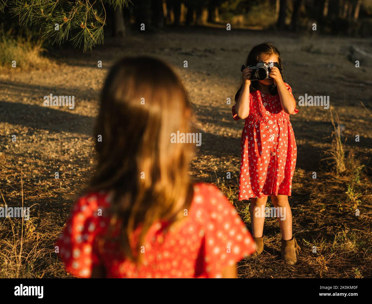 Long haired girl in red dress taking photo of cute little sister in ...