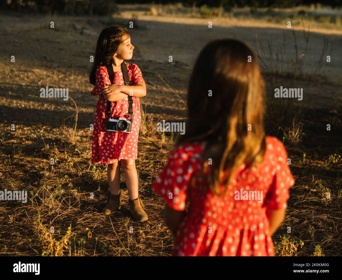Long haired girl in red dress taking photo of cute little sister in ...