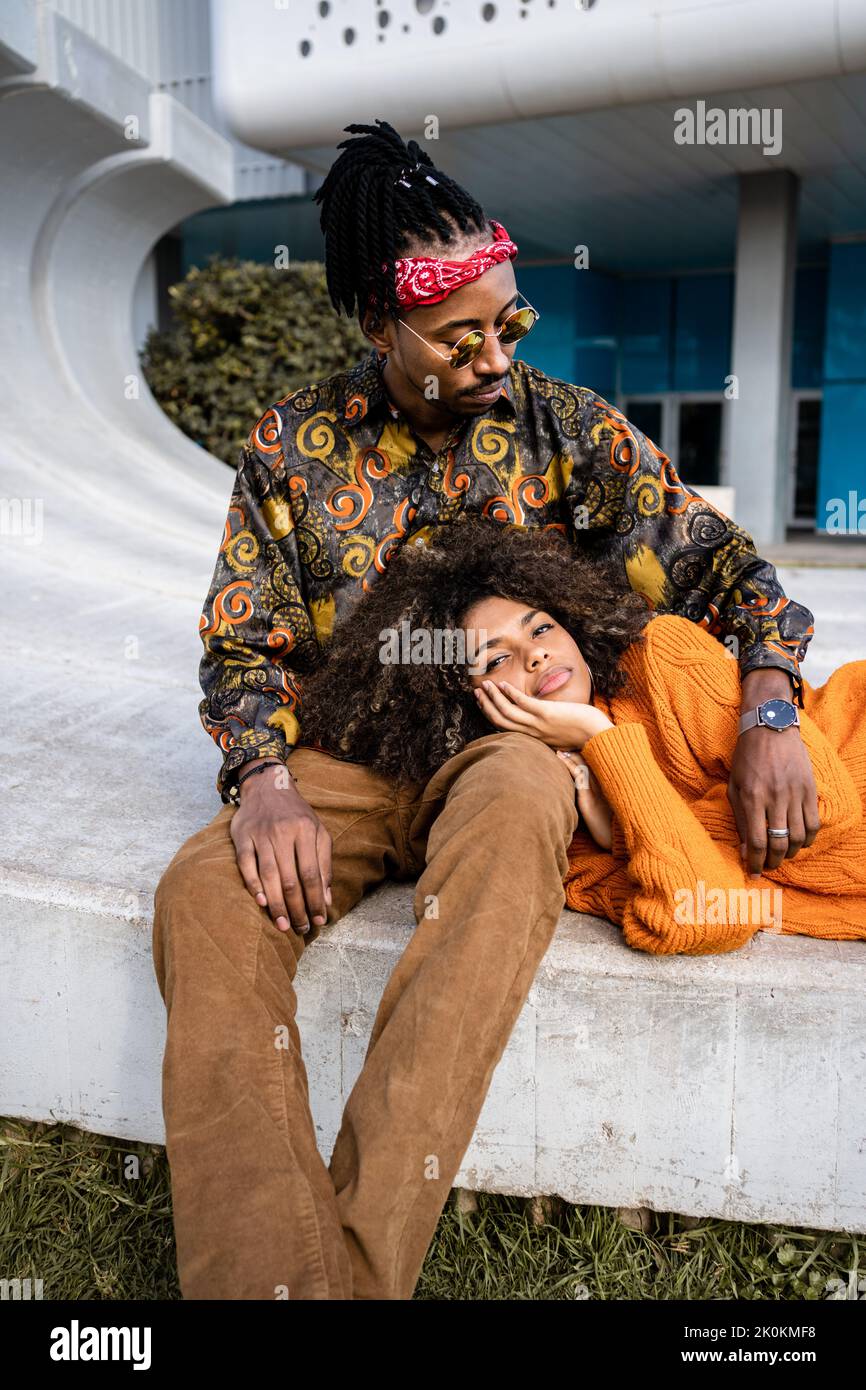Happy black man sitting and woman lying down in stylish casual outfits ...