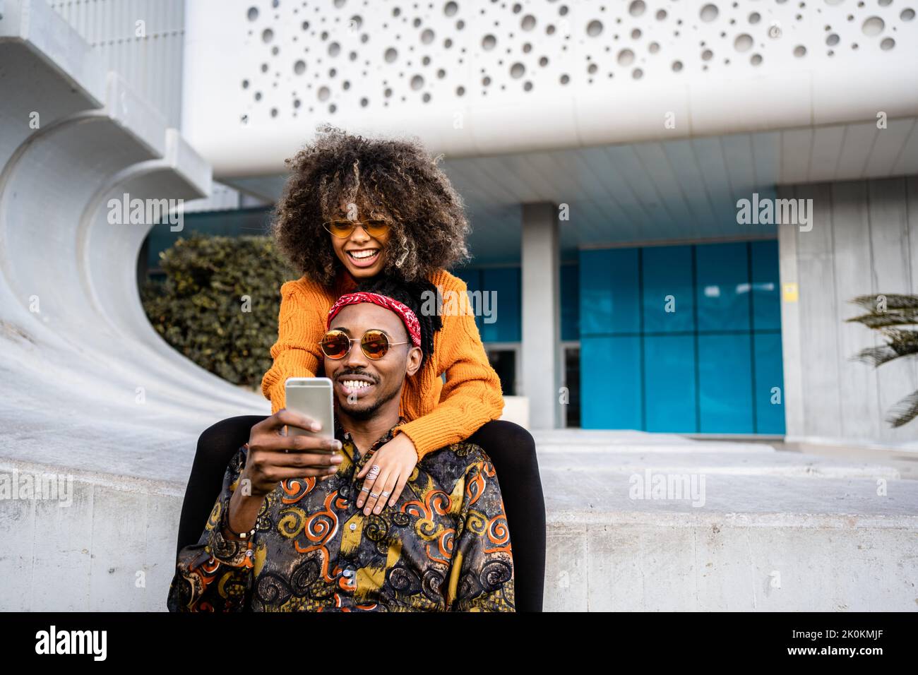Modern black man using mobile phone with charming ethnic woman with Afro hairstyle embracing ...