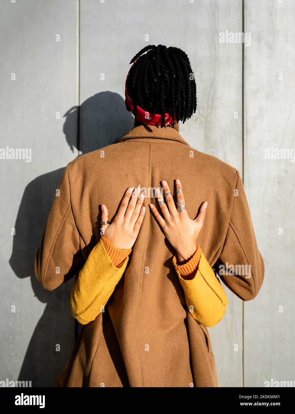 Back view of cool ethnic man with dreadlocks and in coat embracing with ...