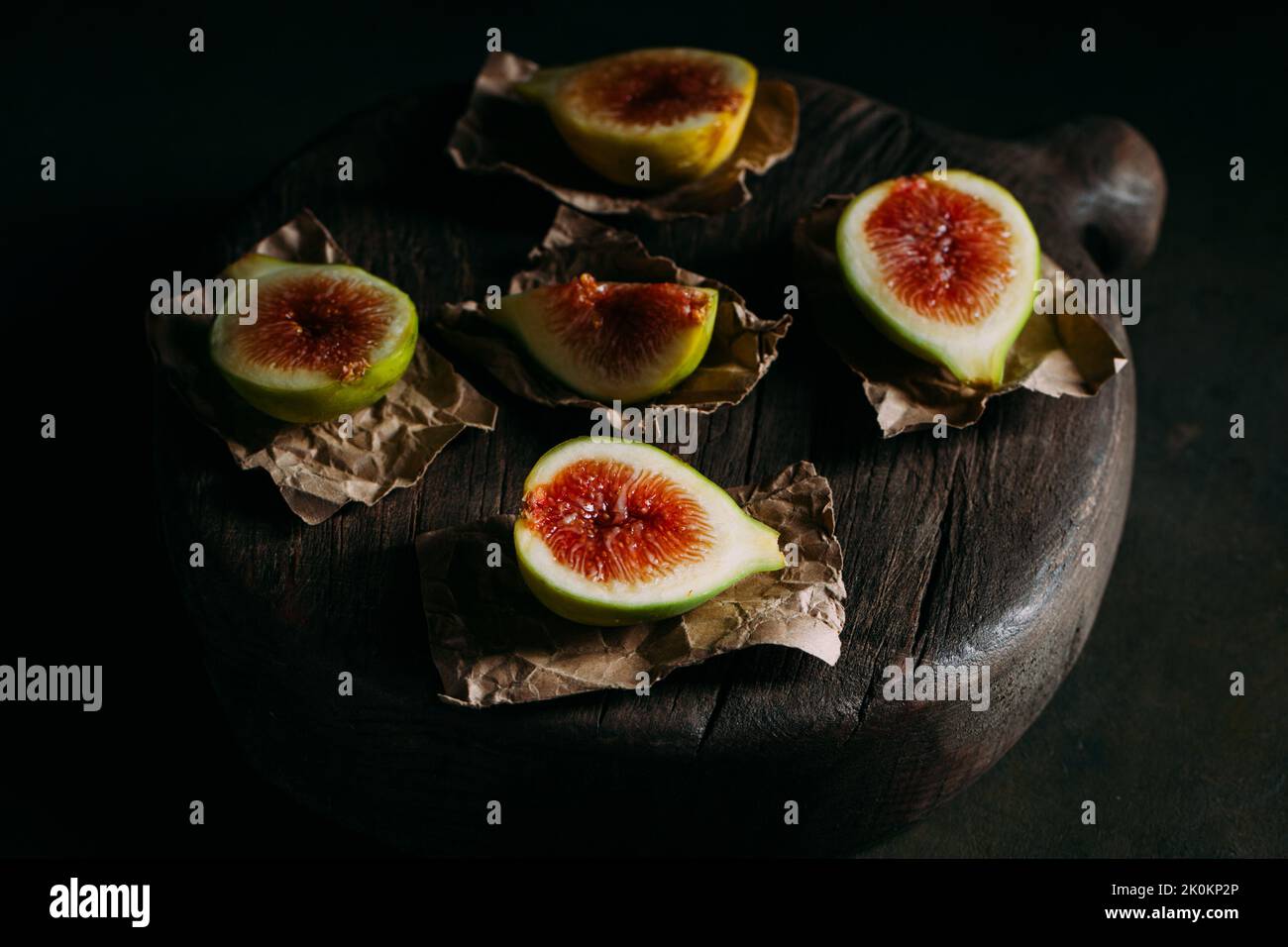 Fresh sweet figs arranged on wooden chopping board on dark background ...