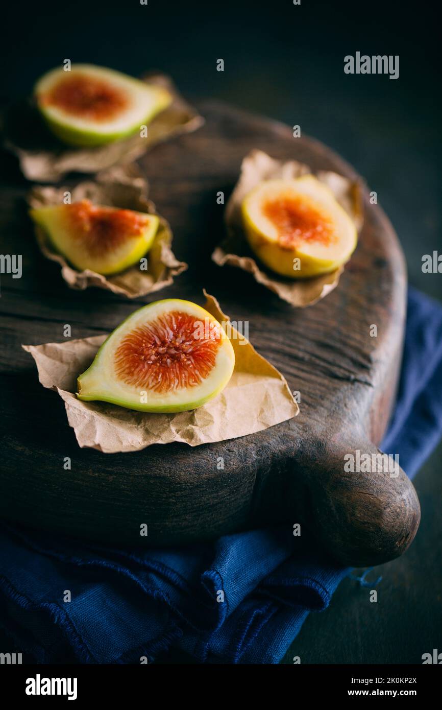 Fresh sweet figs arranged on wooden chopping board on dark background ...