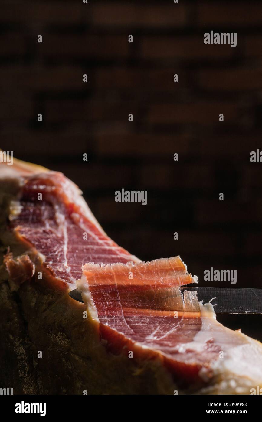 Crop unrecognizable cook cutting slice of tasty dry cured Spanish jamon ...
