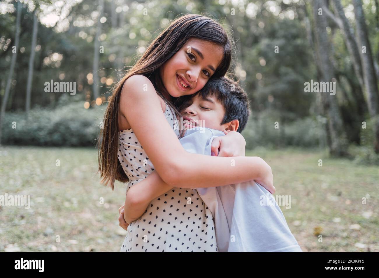 Side view of cheerful girl looking at camera while embracing sibling ...