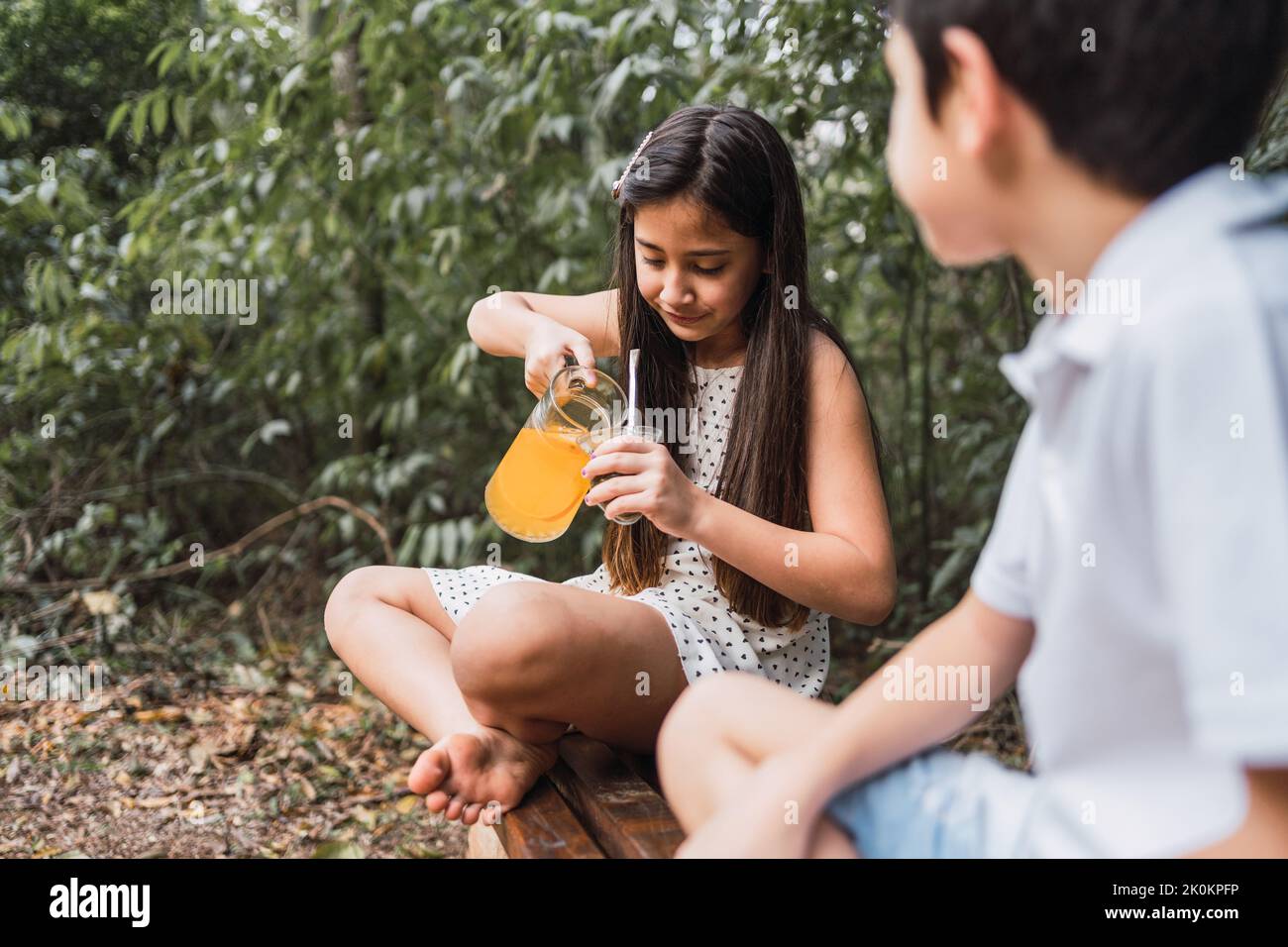 Cheerful child pouring lemonade into calabash gourd while sitting with ...