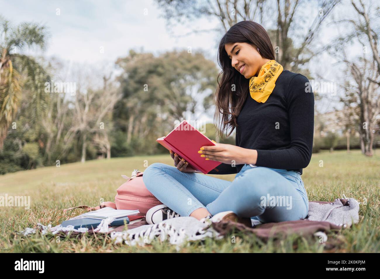 Positive young Hispanic female student in denim clothes reading book ...