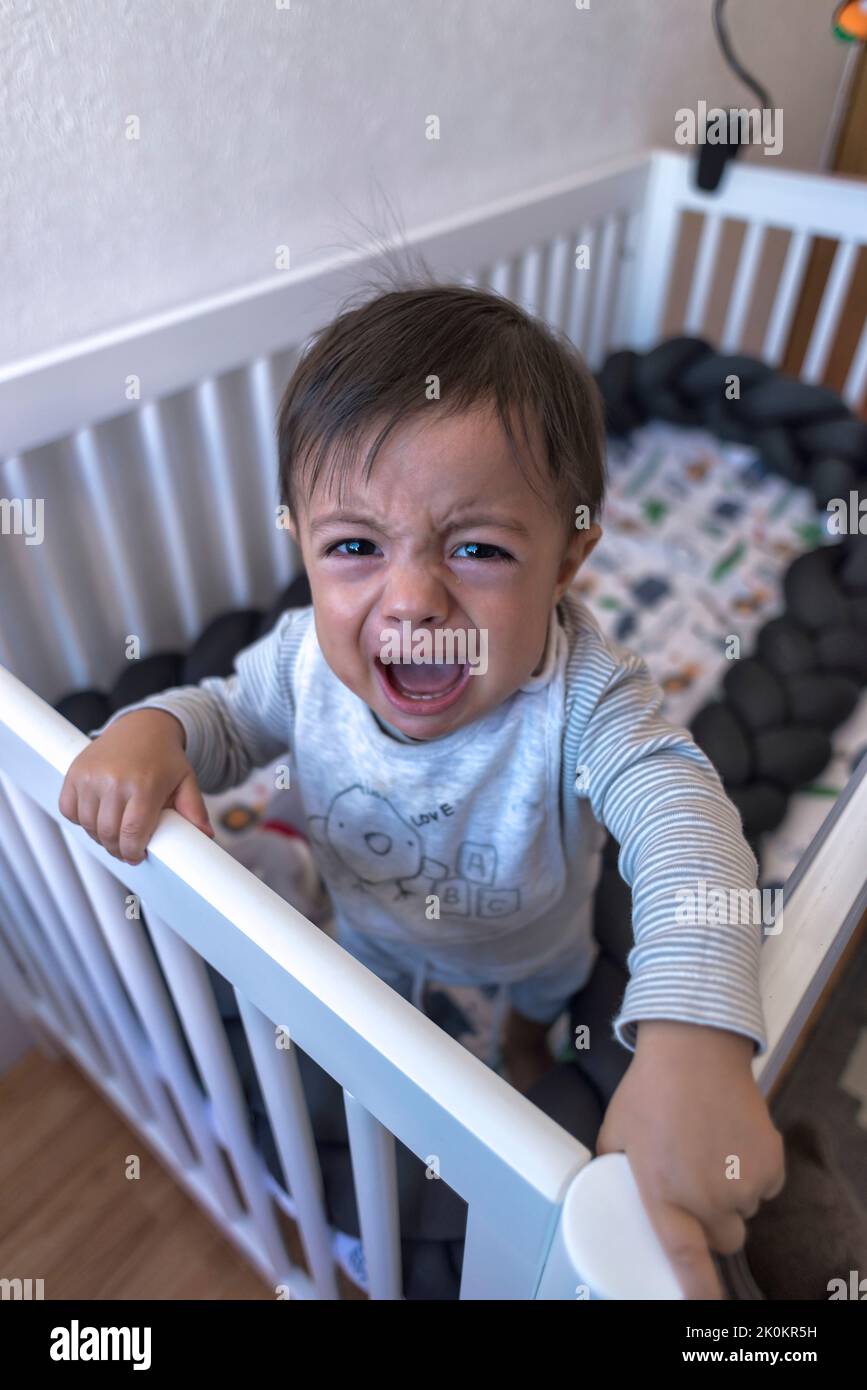 High angle of cute ethnic boy screaming loud with opened mouth in crib ...