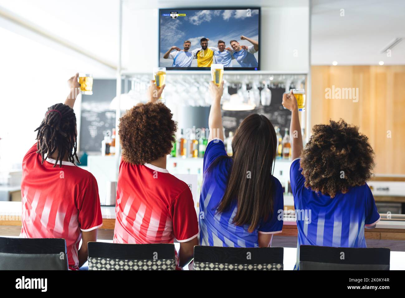 Group of diverse friends sitting in the bar, drinking beer and watching ...