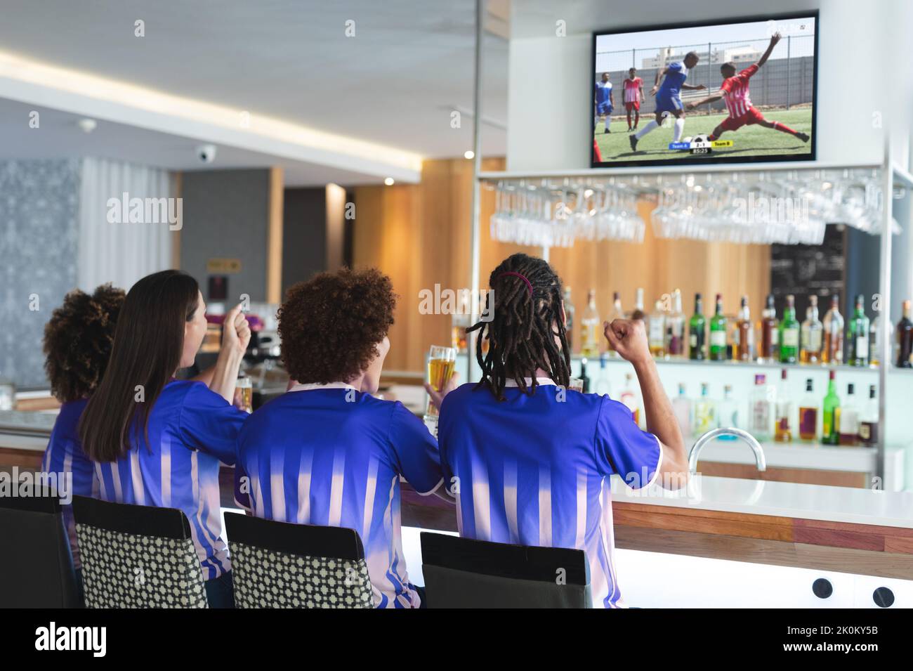 Group of diverse friends sitting in the bar, drinking beer and watching ...