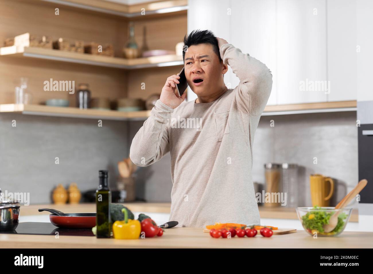 Shocked asian man cooking meal and talking on phone Stock Photo - Alamy