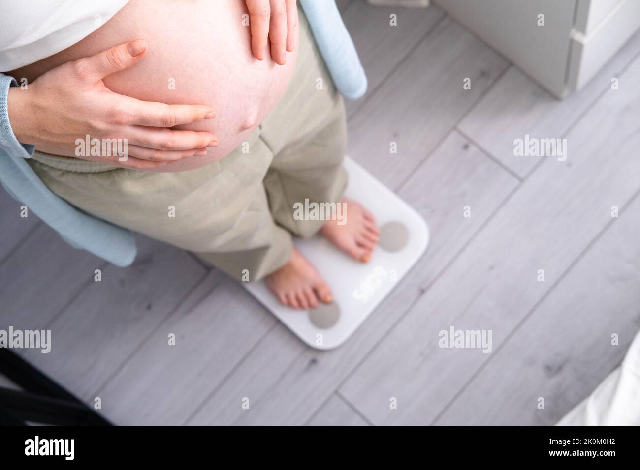 Young Woman Measuring Her Pregnant Weight Standing On Scales