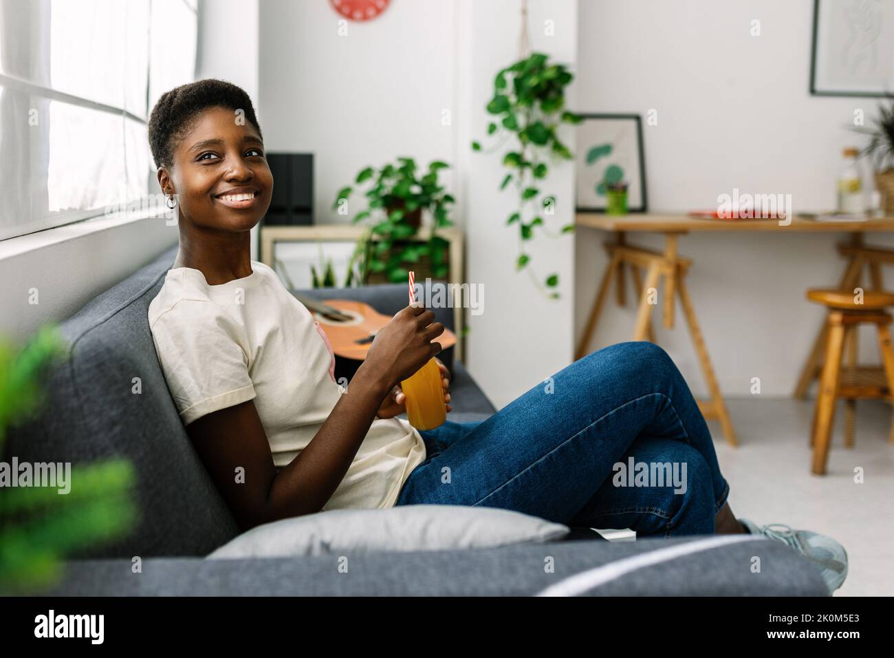 Young african woman chilling on sofa drinking orange juice Stock Photo ...