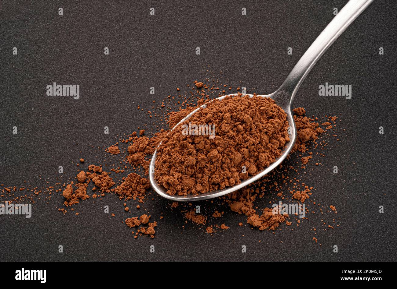 Cocoa powder in spoon on black background Stock Photo - Alamy