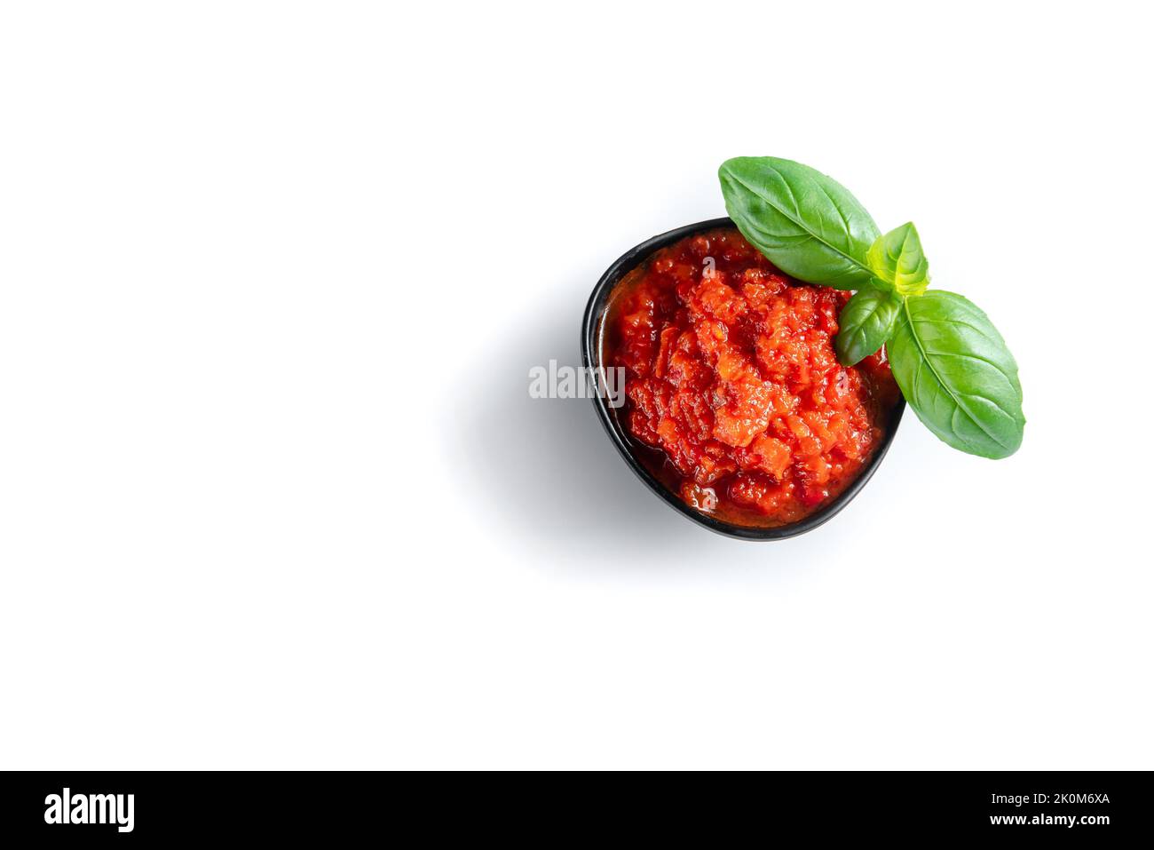 Ajvar in a black pial with basil on a white background. Isolate. Sweet ...
