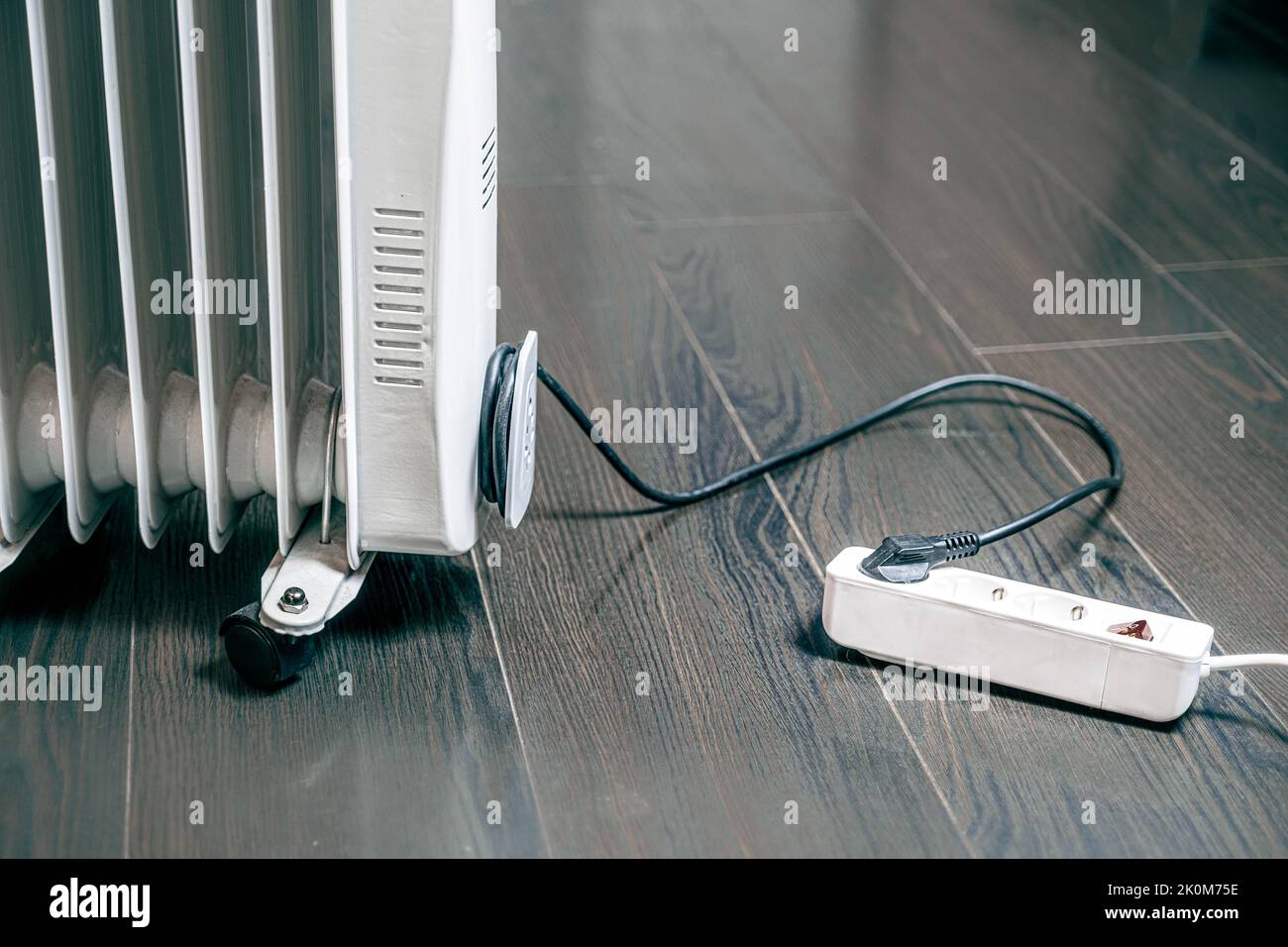 oil electric heater on a wooden floor is plugged into a socket ...