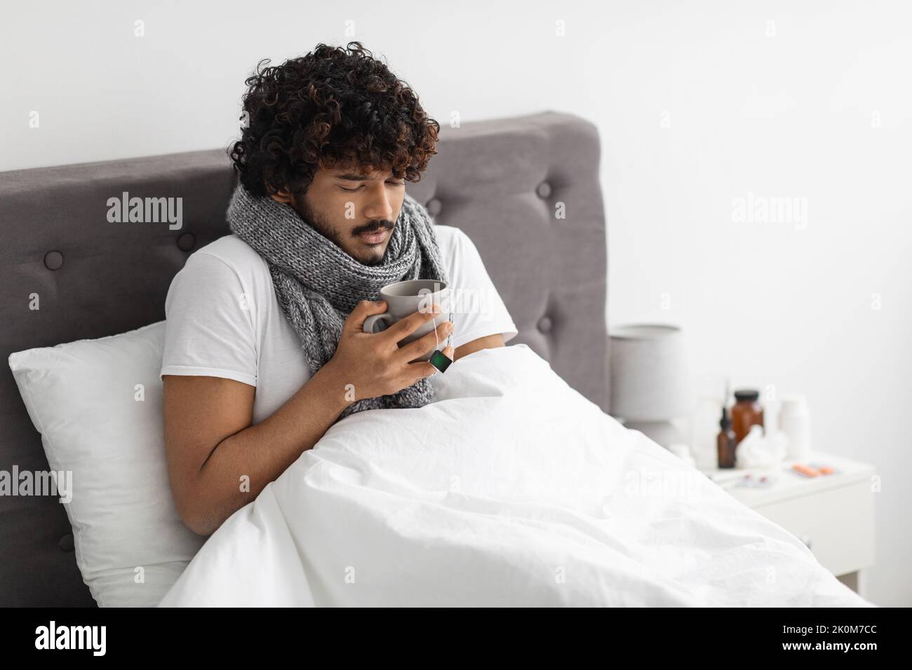 Sick indian guy staying in bed, having hot drink Stock Photo - Alamy