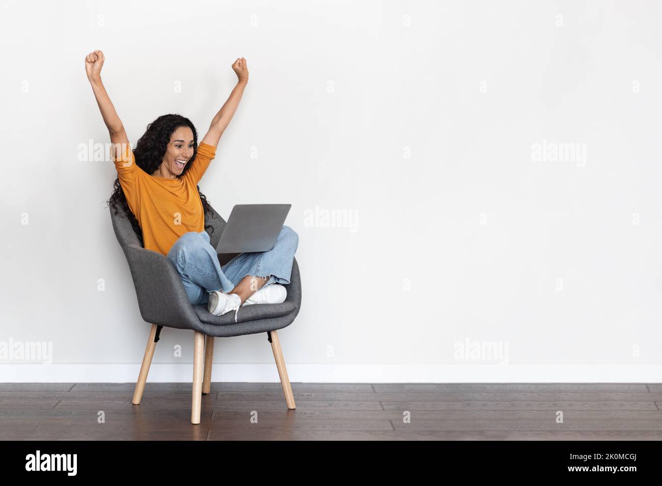 Happy woman with computer on her lap raising hands up Stock Photo - Alamy