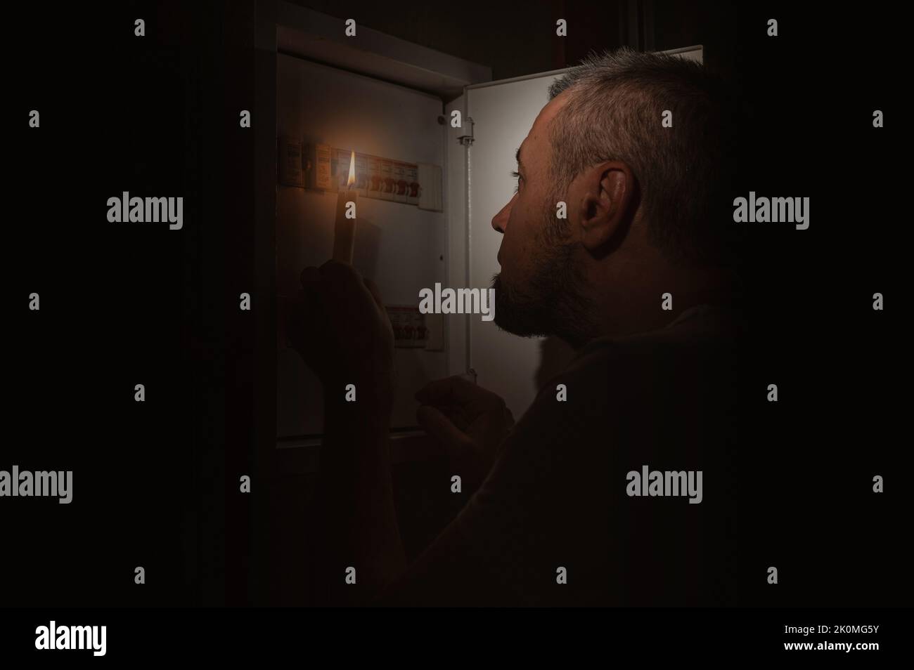 Blackout, No electricity. A man with a candle in the dark examines the ...