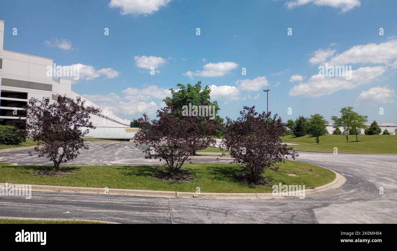 A curve street with trees in the middle and a cloudy blue sky Stock ...