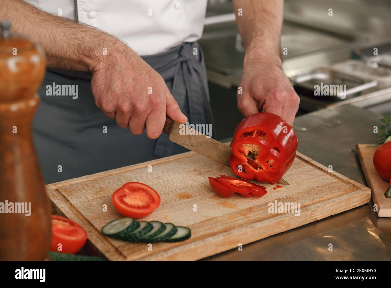 Busy chef cutting red pepper and cucumbers on a board for making salad ...