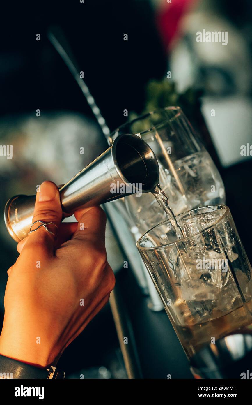 A vertical closeup of the hand of barman pouring a cocktail into a ...