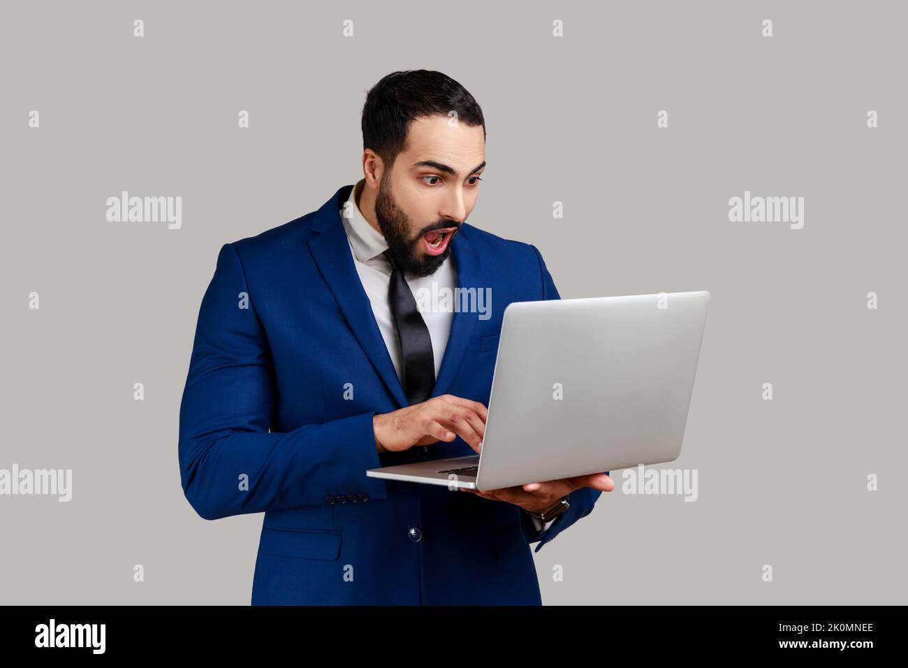 Surprised bearded man holding laptop, typing on keyboard, surfing ...