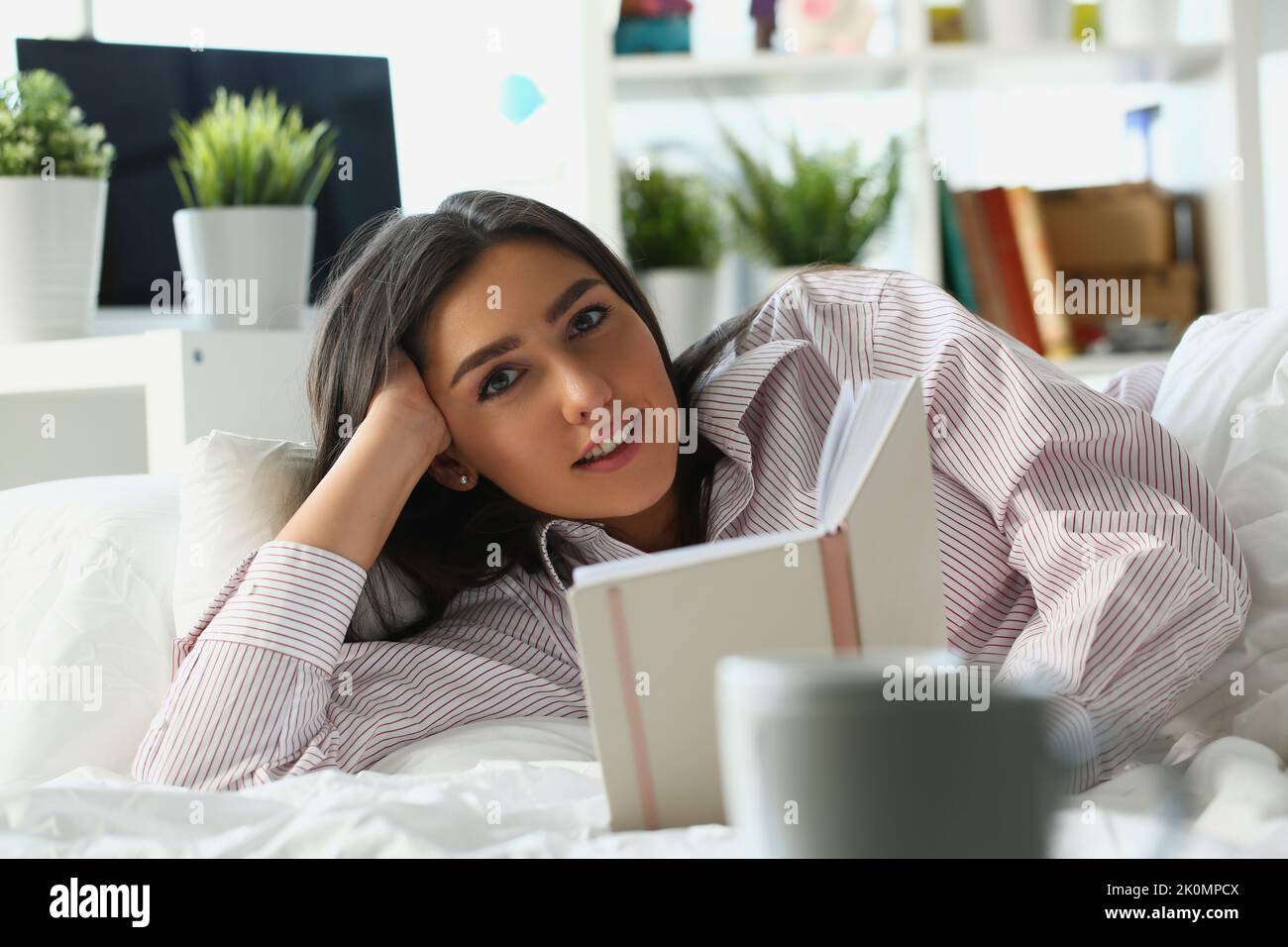 Beautiful woman lies in bed and reads book Stock Photo - Alamy