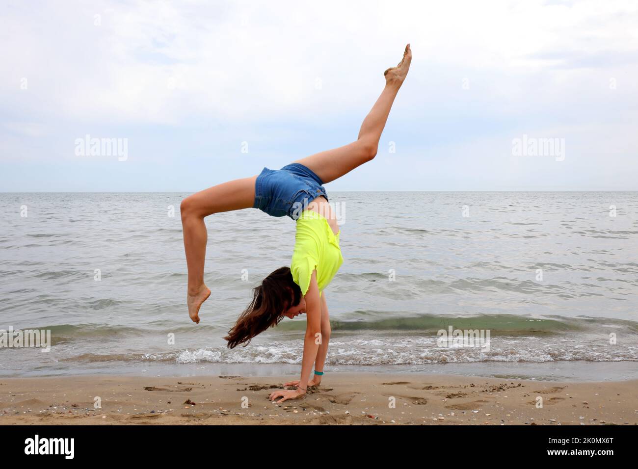 slender girl on the foreshore of the sea while performing gymnastic ...
