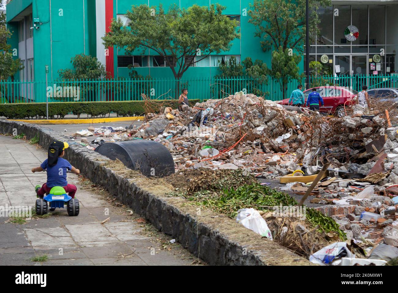 A kid riding a tricycle and looking at a building collapsed building ...