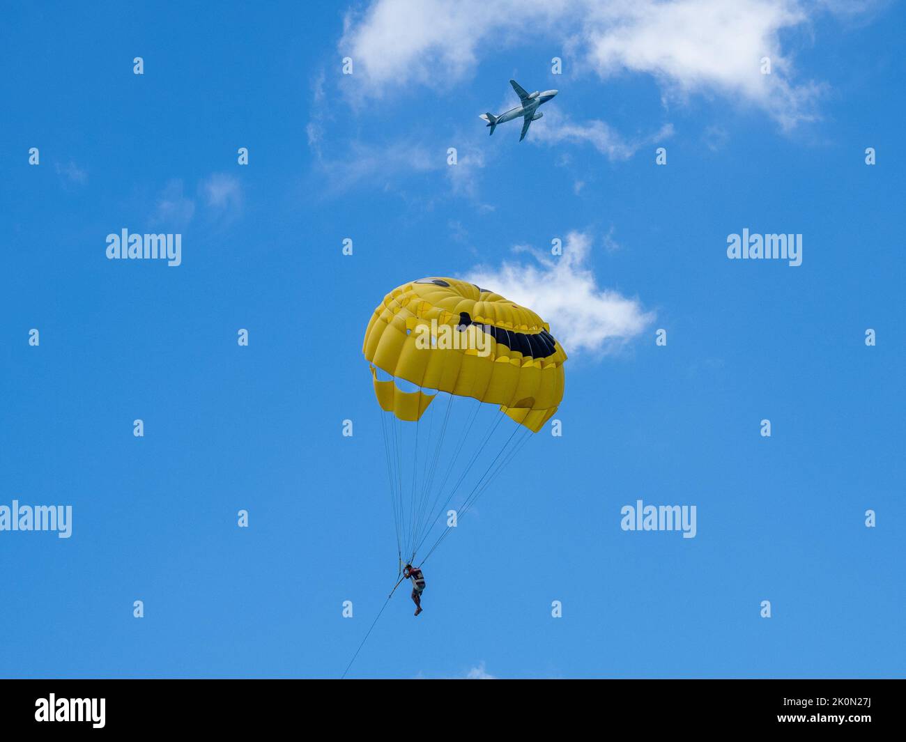 A parachuter in the blue sky with an airplane gaining altitude over the ...