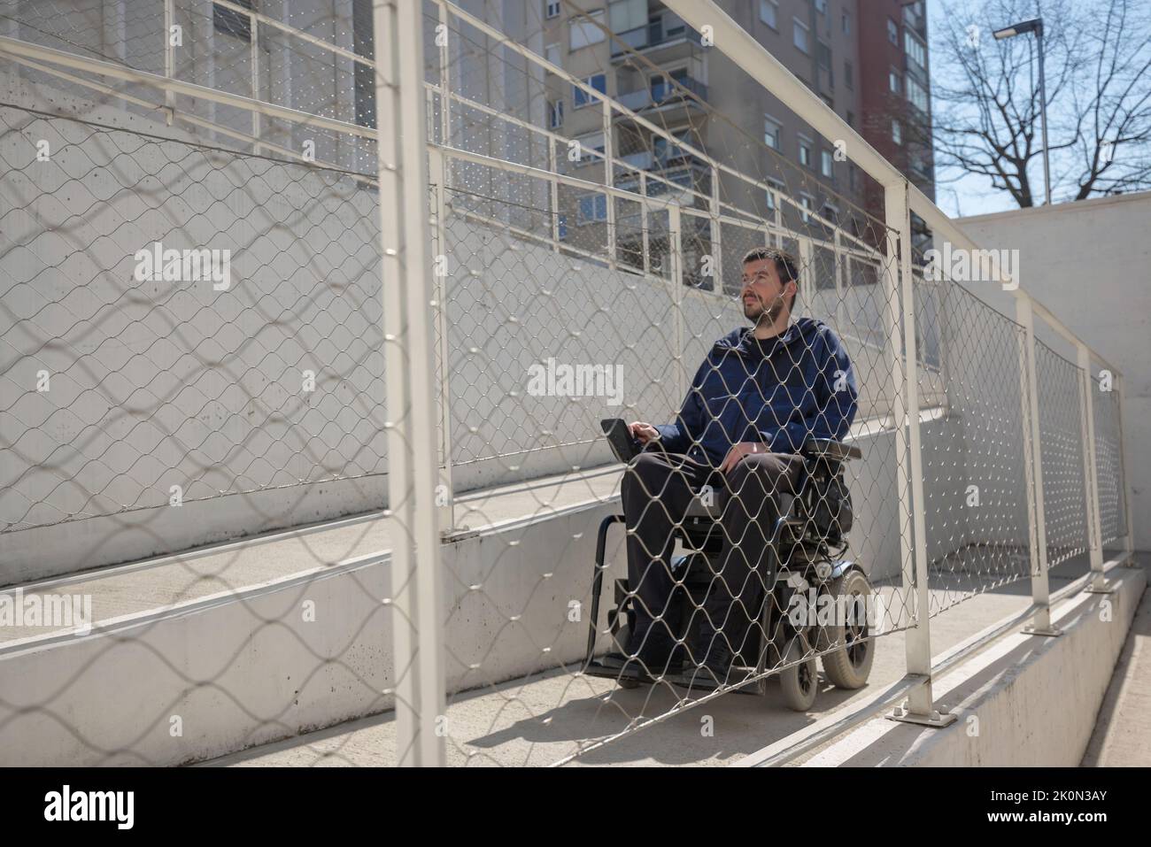 Man on electric wheelchair moving along concrete accessibility pathway ...