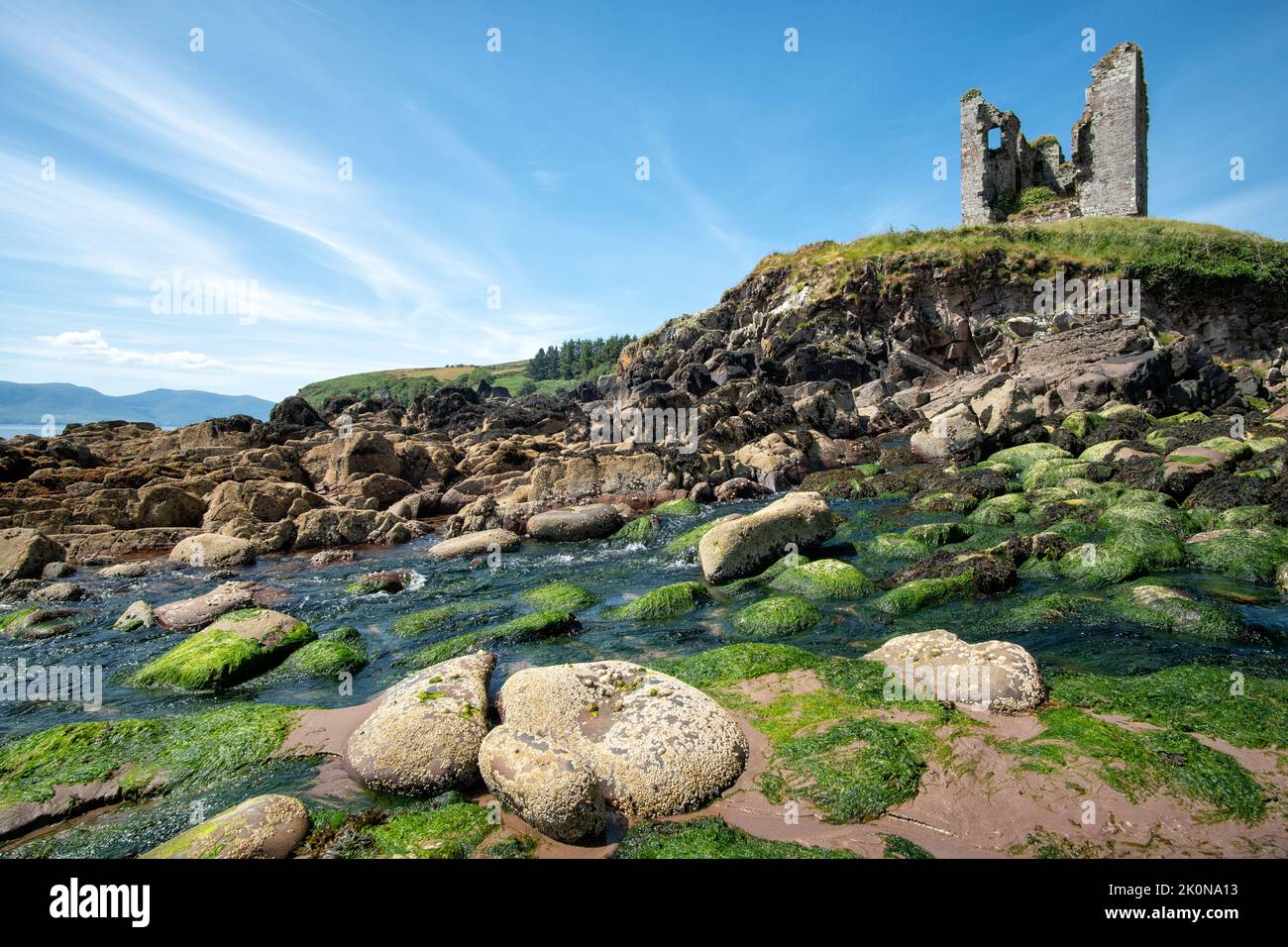 Blue sky above the ruins of Minard Castle seen from the rocky beach of ...