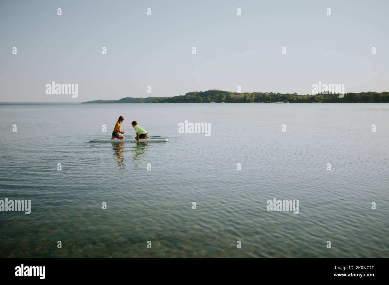Two brothers sitting on a paddle board on a serene lake Stock Photo - Alamy