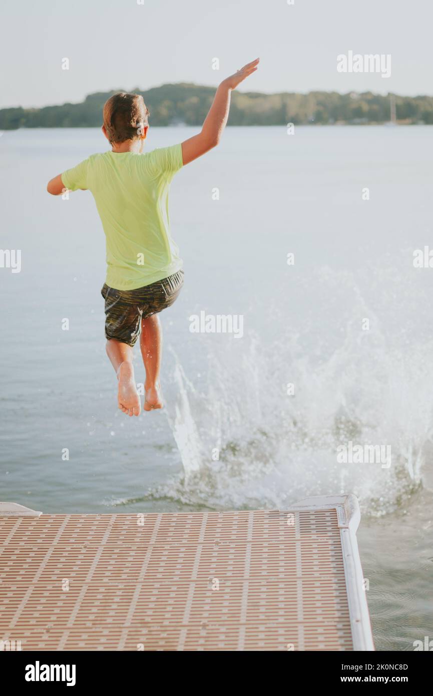 Boy in green swim shirt jumps off dock into lake with splash below ...