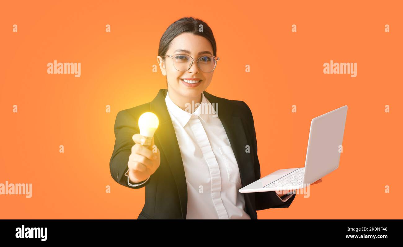 Businesswoman with laptop and glowing light bulb on orange background ...
